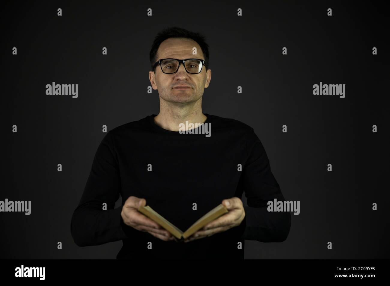 Smart man in casual wear and glasses holds old open book and looks at ...