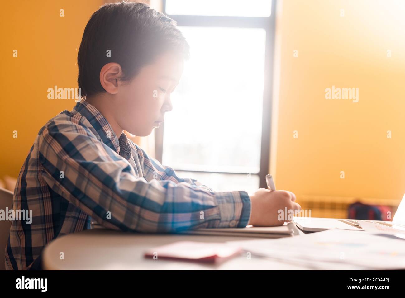 asian boy writing and studying at home with sunlight during quarantine ...