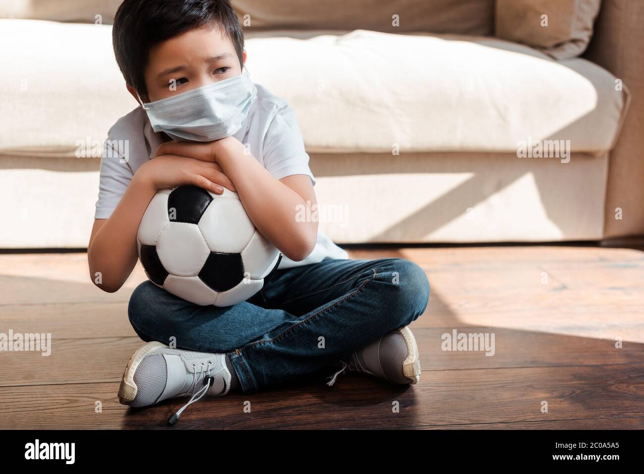 sad asian kid with football ball sitting on floor at home on self ...
