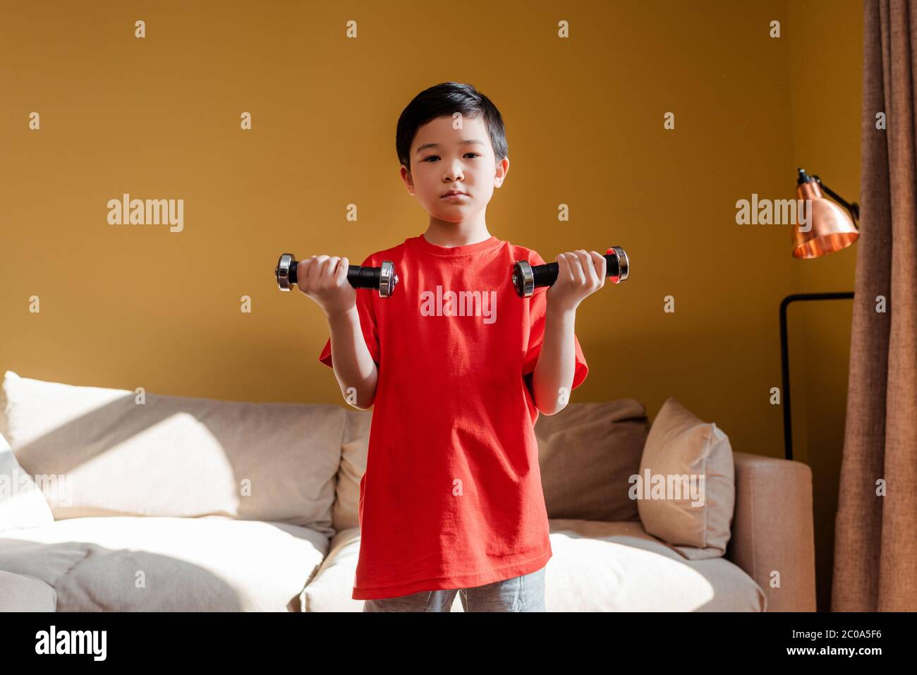 sportive asian boy exercising with dumbbells at home during self ...