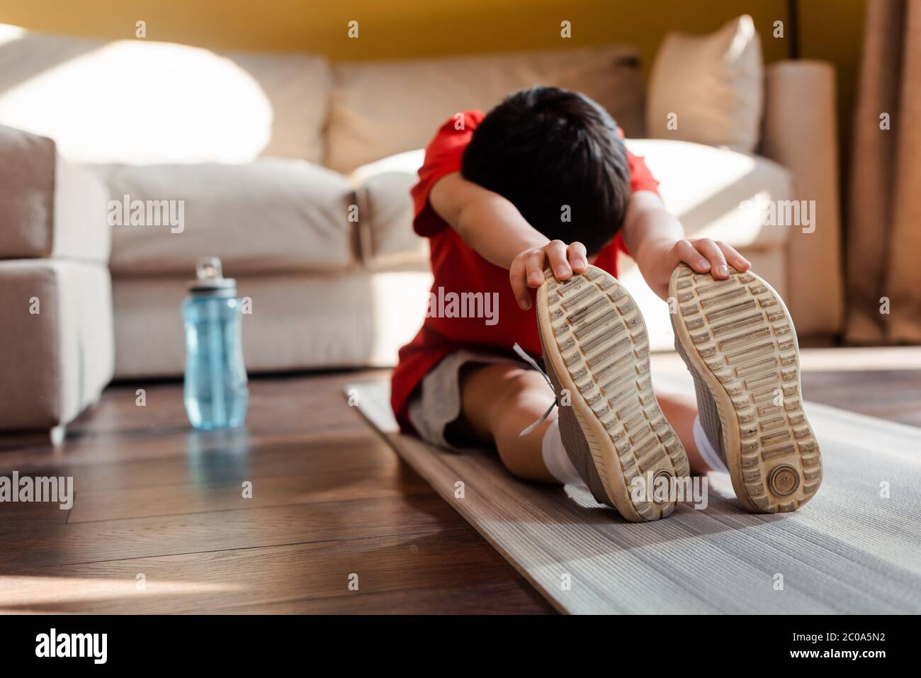 sportive asian boy stretching on fitness mat with sports bottle at home ...