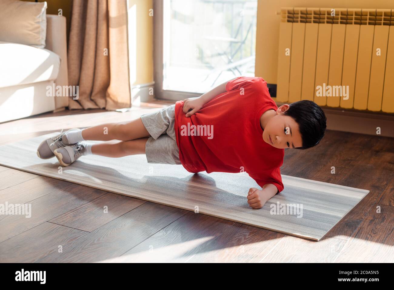 sportive asian kid doing side plank on fitness mat at home during self ...