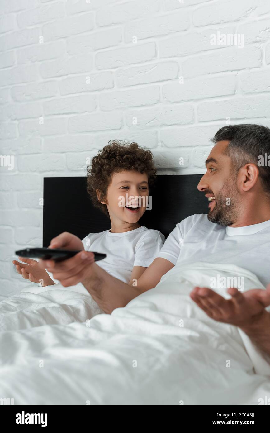 selective focus of cheerful father holding remote controller near happy ...