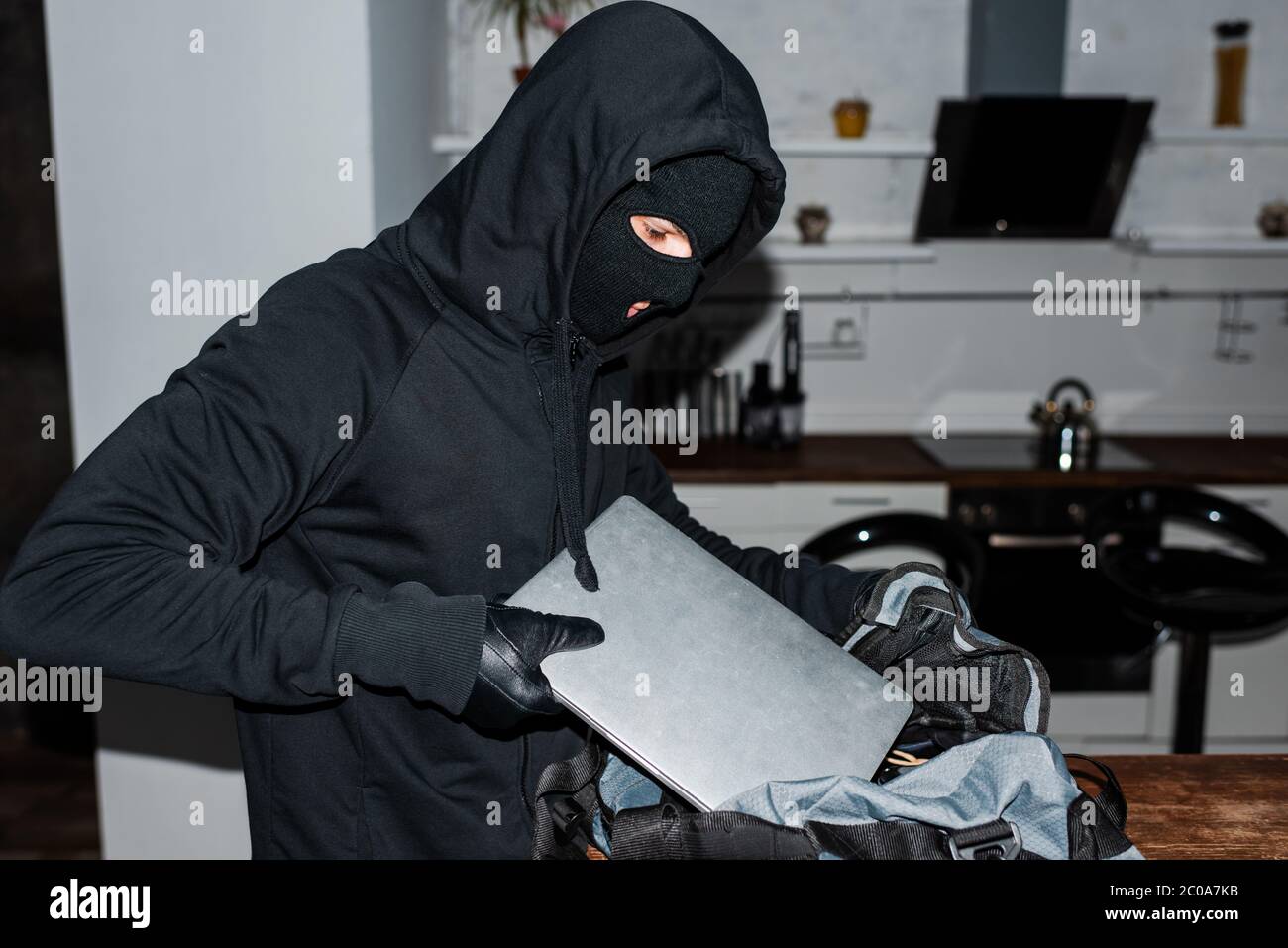 Robber in balaclava putting laptop in bag during stealing Stock Photo ...