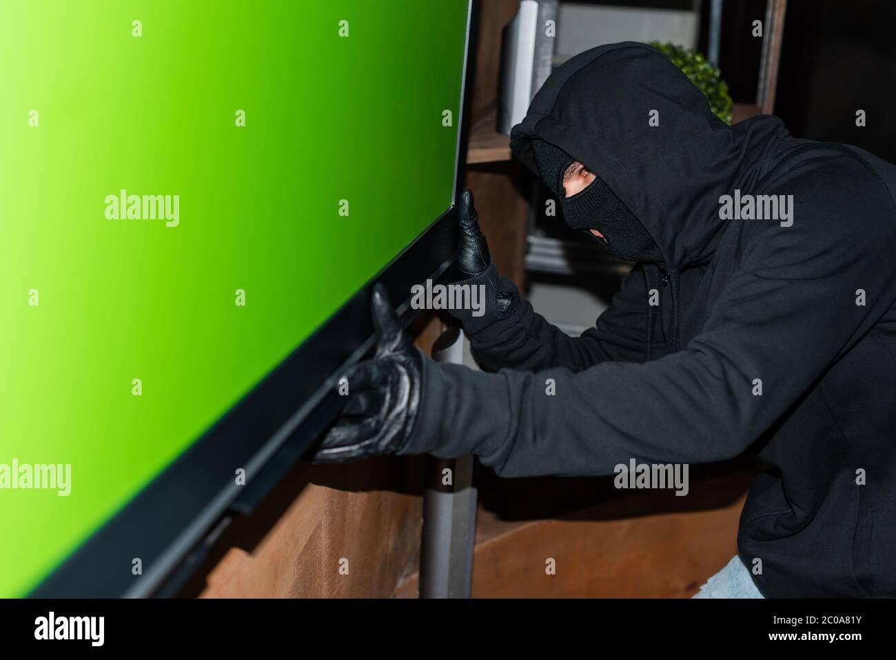 Side view of robber in mask and leather gloves holding tv during ...