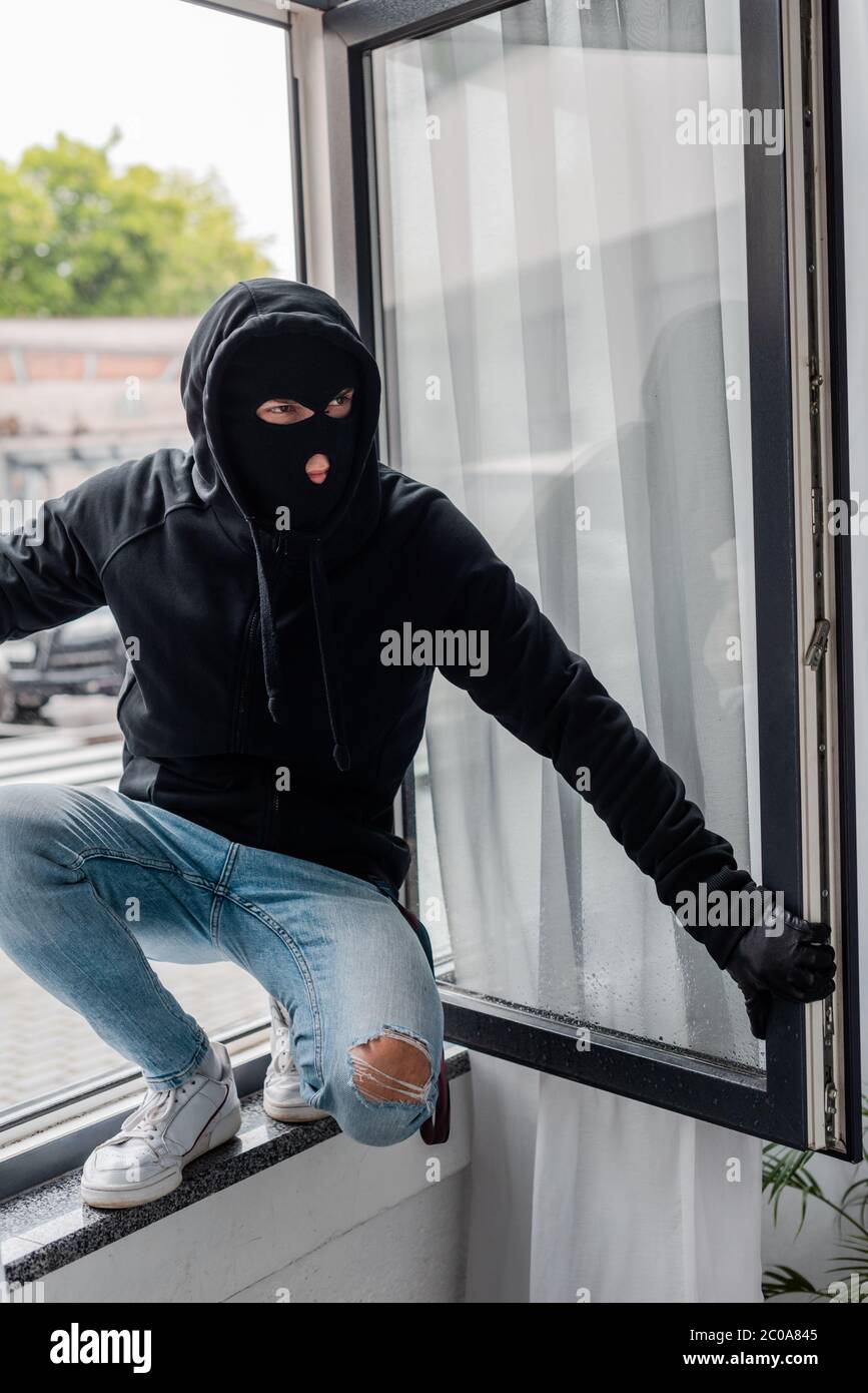 Robber in balaclava standing on open window during stealing Stock Photo ...