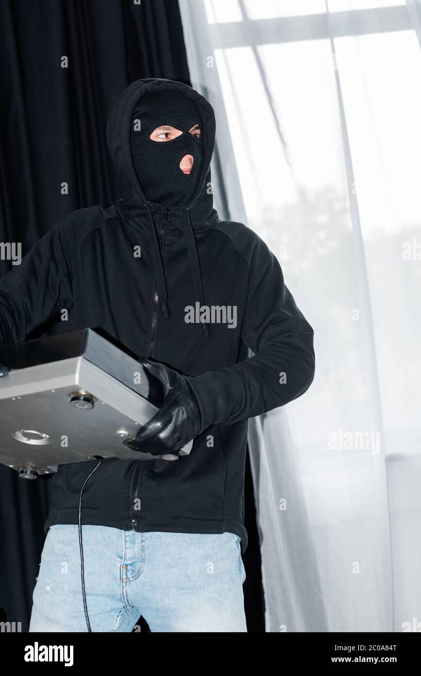 Robber in balaclava and leather glove holding record player during ...