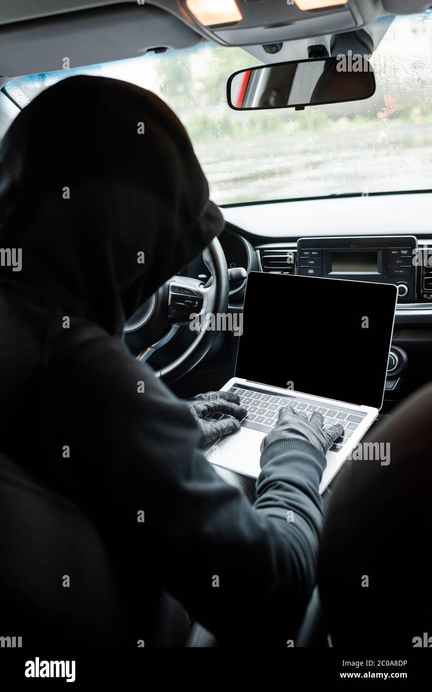 Back view of burglar in leather gloves using laptop with blank screen ...