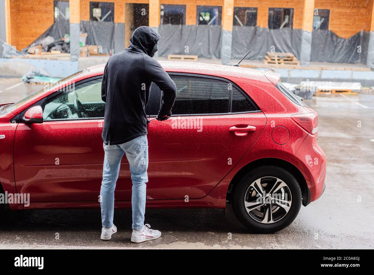 Back view of robber looking away while opening car door with ...
