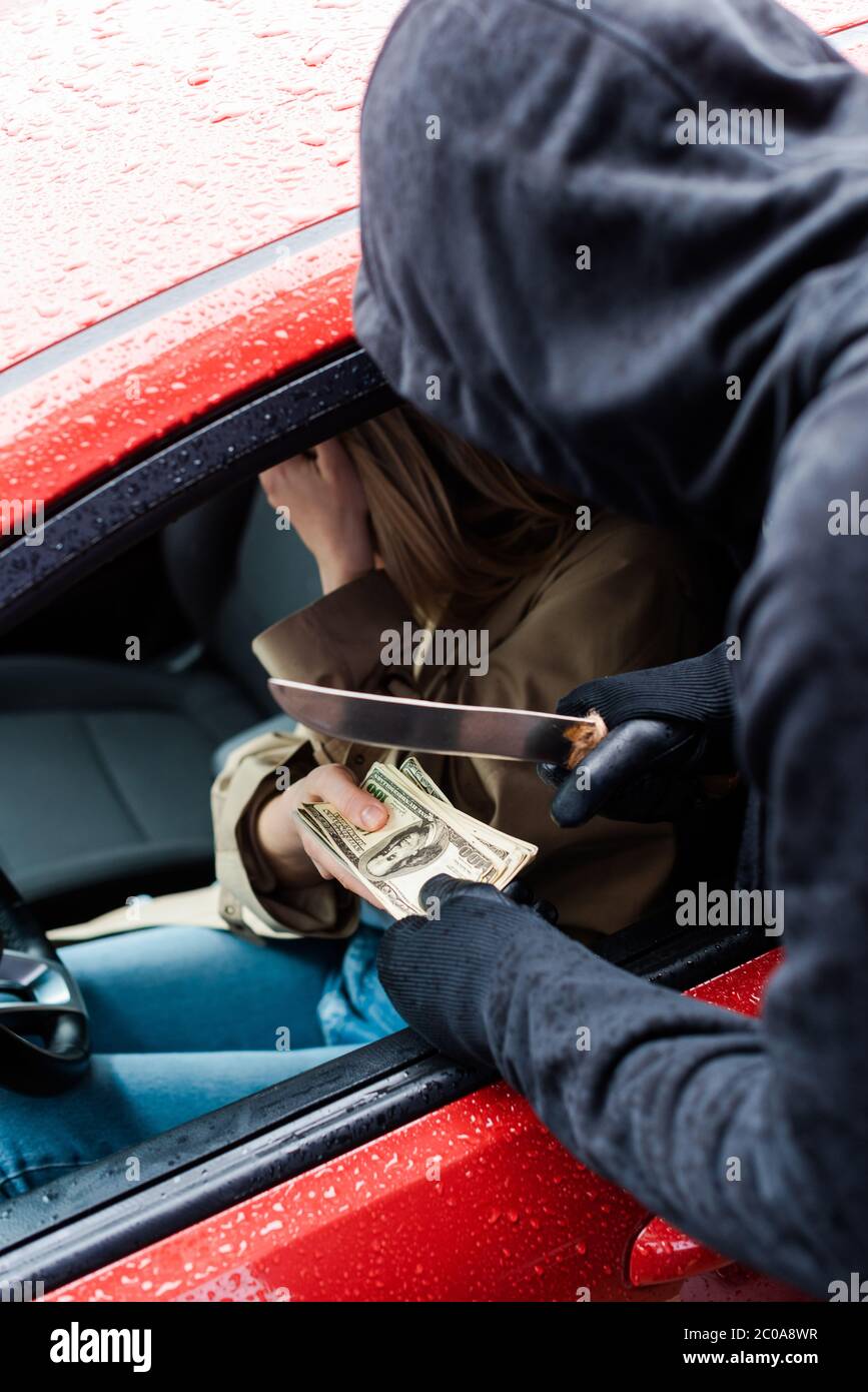 Selective focus of robber holding knife and dollars near scared driver ...