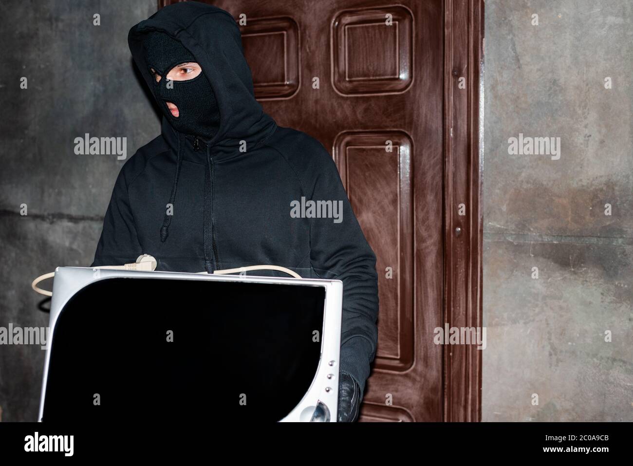 Robber in balaclava holding microwave oven during house stealing Stock ...
