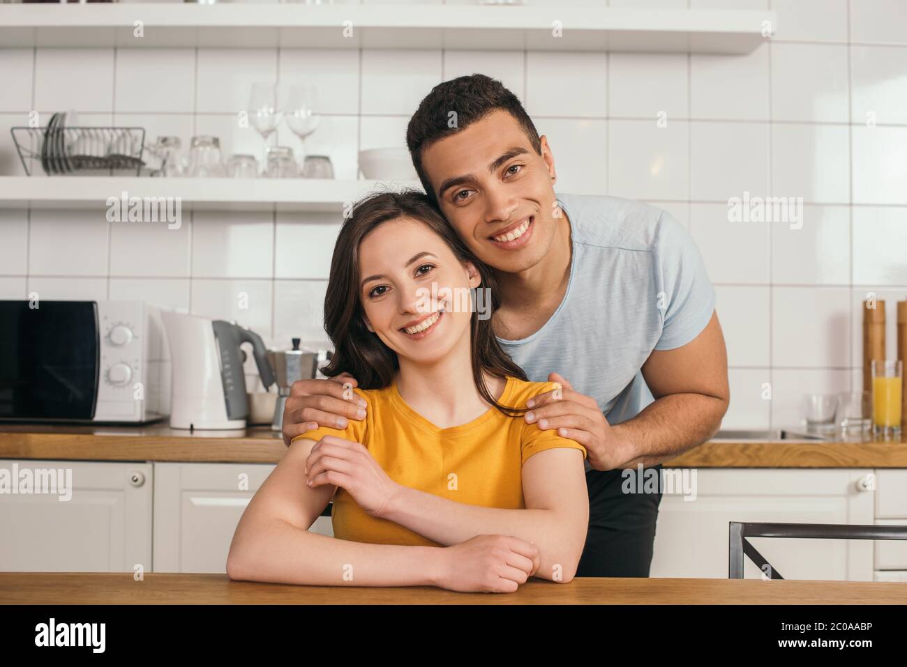cheerful mixed race man hugging attractive girl in kitchen Stock Photo ...