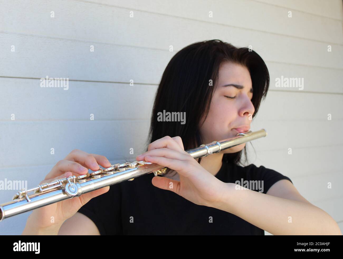 Black-haired girl plays the flute outside in front of a white ...