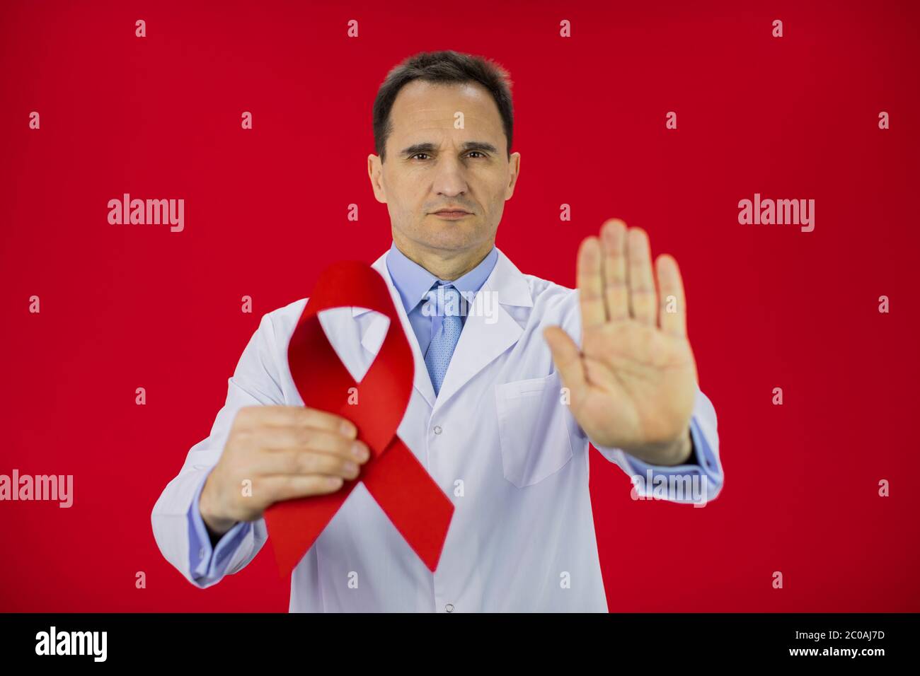 Serious doctor in lab coat with red ribbon shows stop sign on red ...