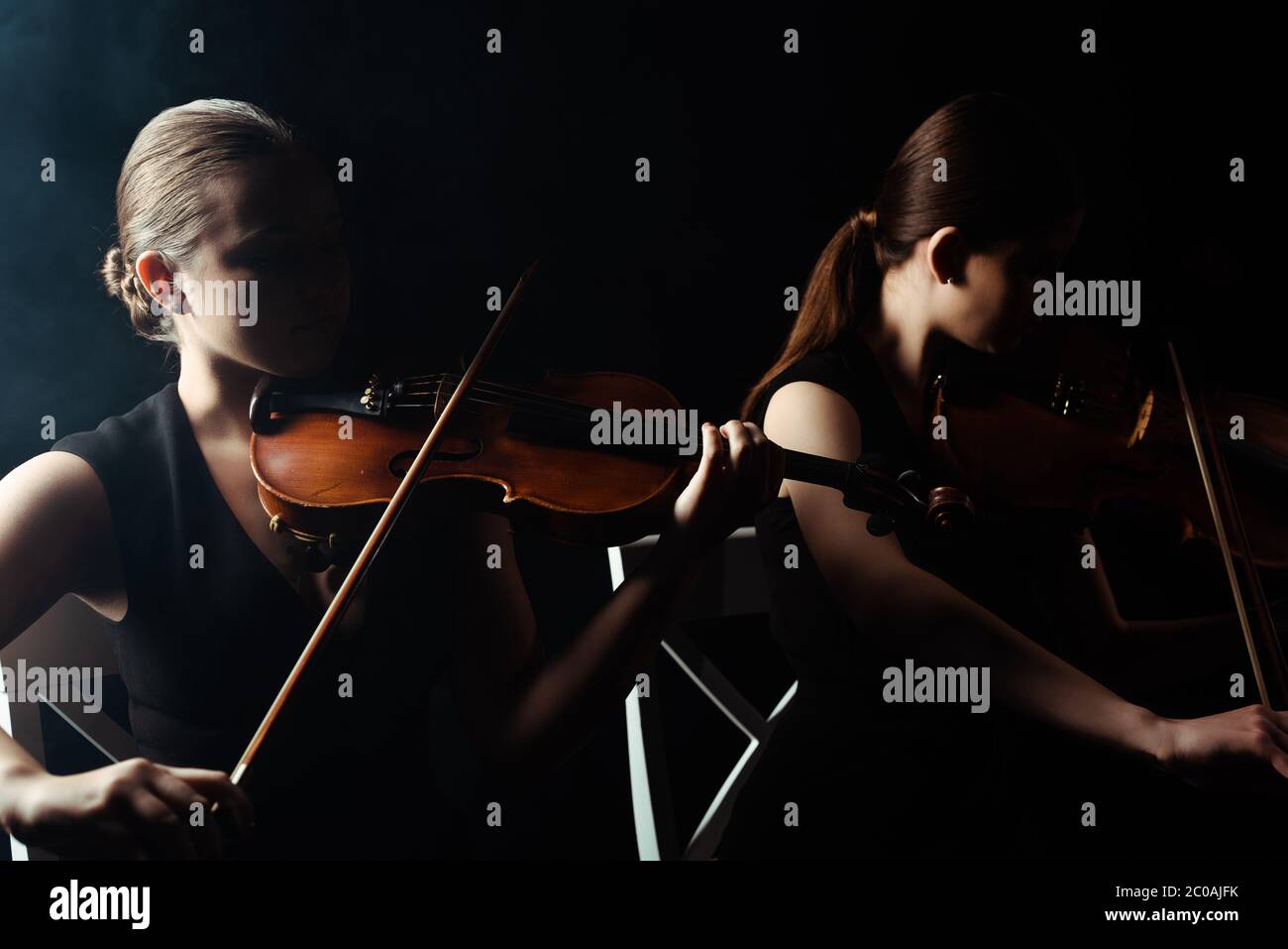 two musicians playing classical music on violins on dark stage Stock ...