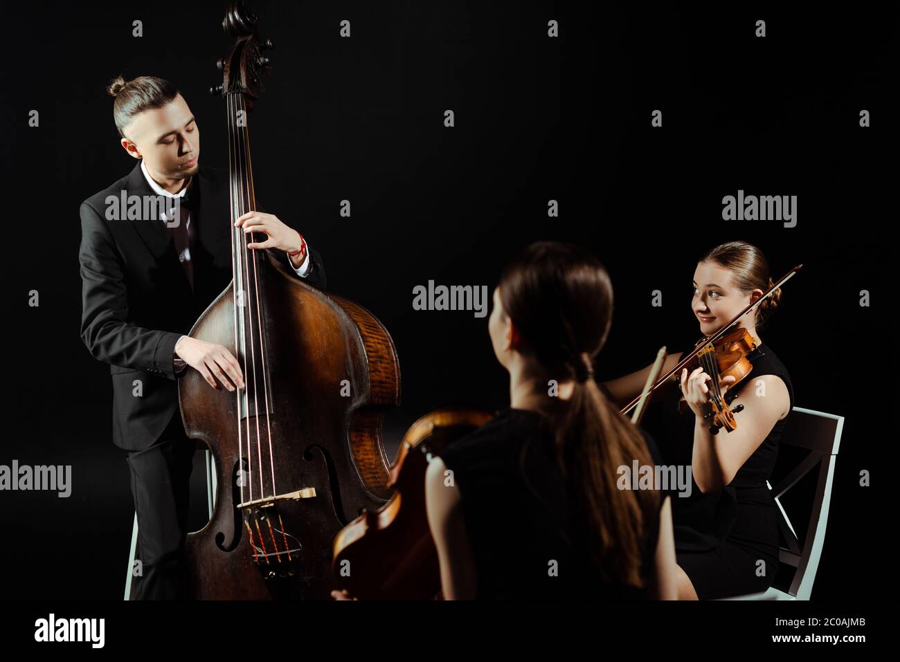 trio of musicians playing on double bass and violins isolated on black ...