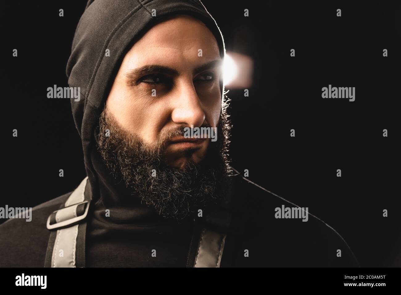 Bearded muslim terrorist looking away on black background with lighting ...