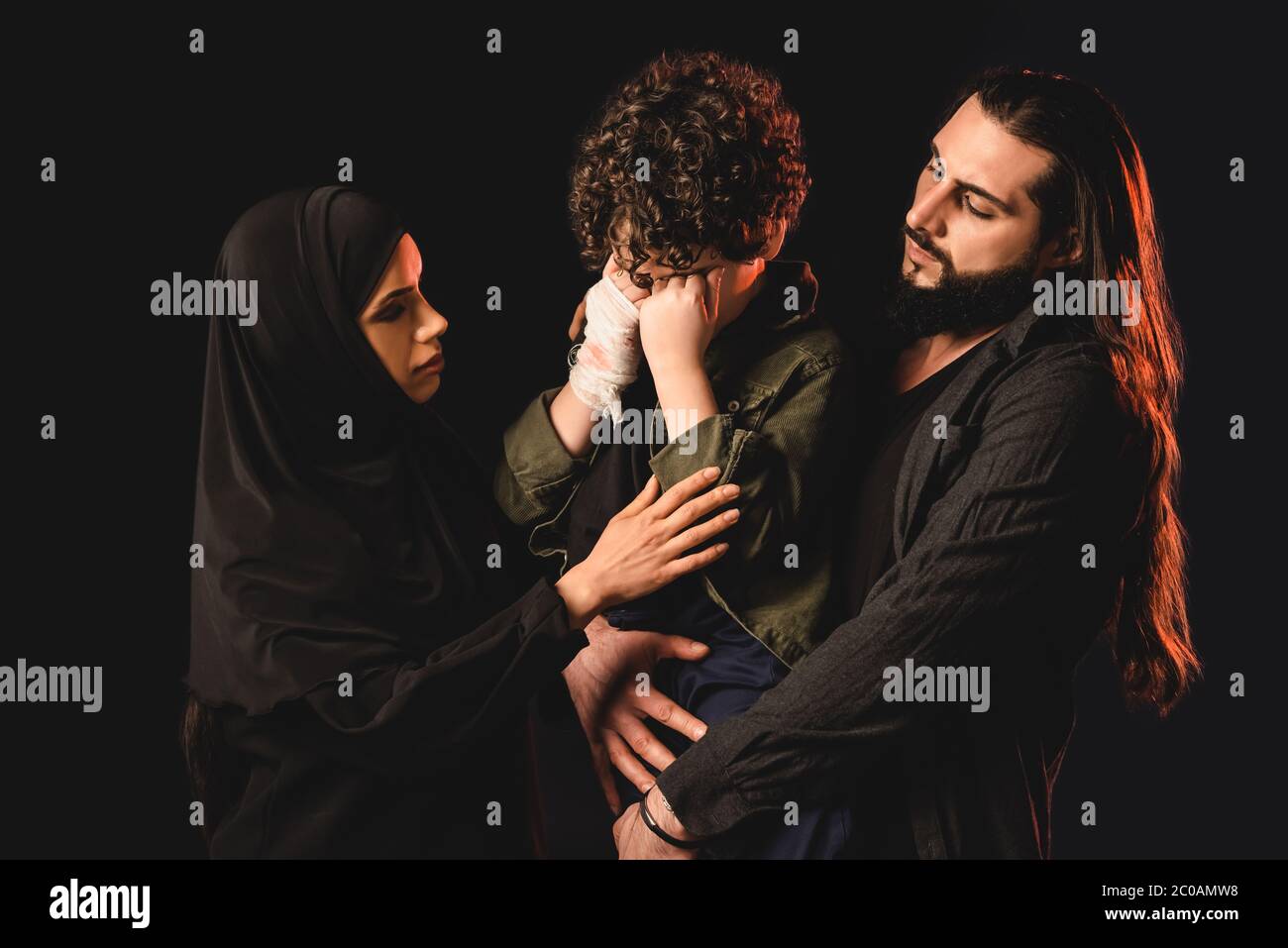 Muslim parents embracing crying son with injured hand isolated on black ...