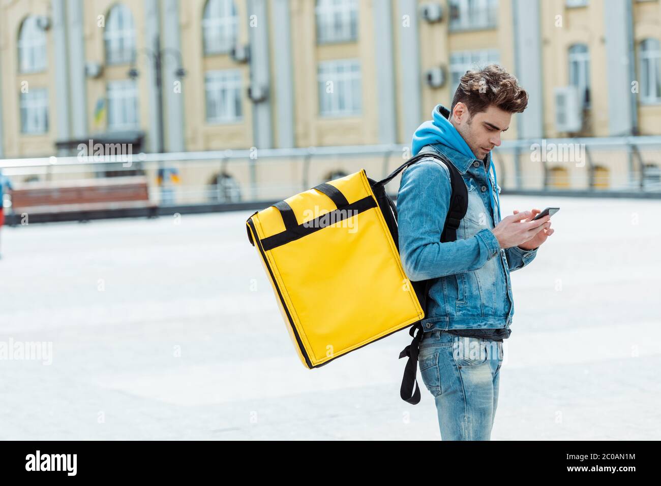 Side view of delivery man using cellphone while standing on urban ...