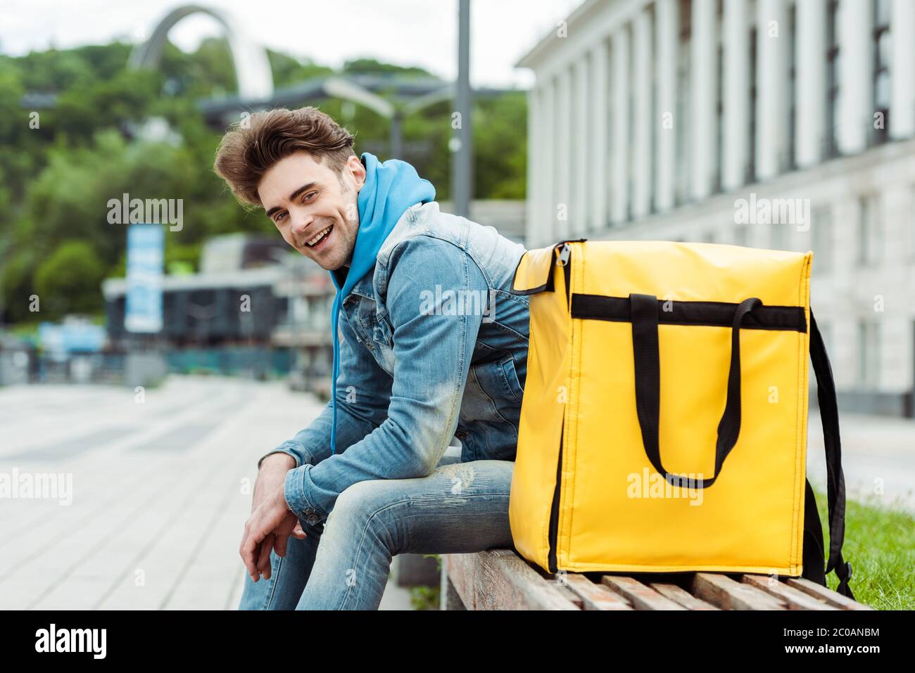 Side view of handsome courier smiling while sitting near thermo bag on ...