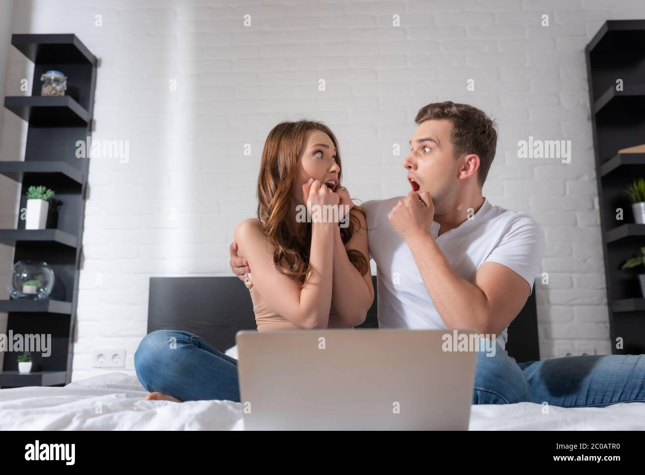 scared couple looking at each other near laptop in bedroom Stock Photo - Alamy