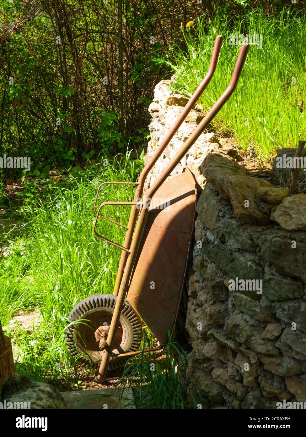 Old rusty garden wheelbarrow leaned on the wall after work Stock Photo ...