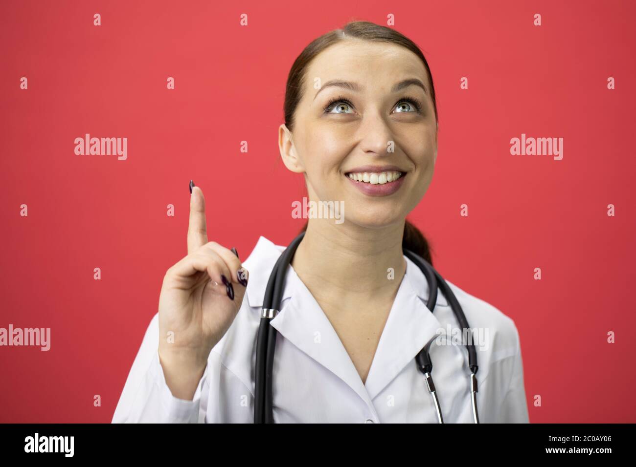 Excited attractive doctor points up with finger to text space on red ...