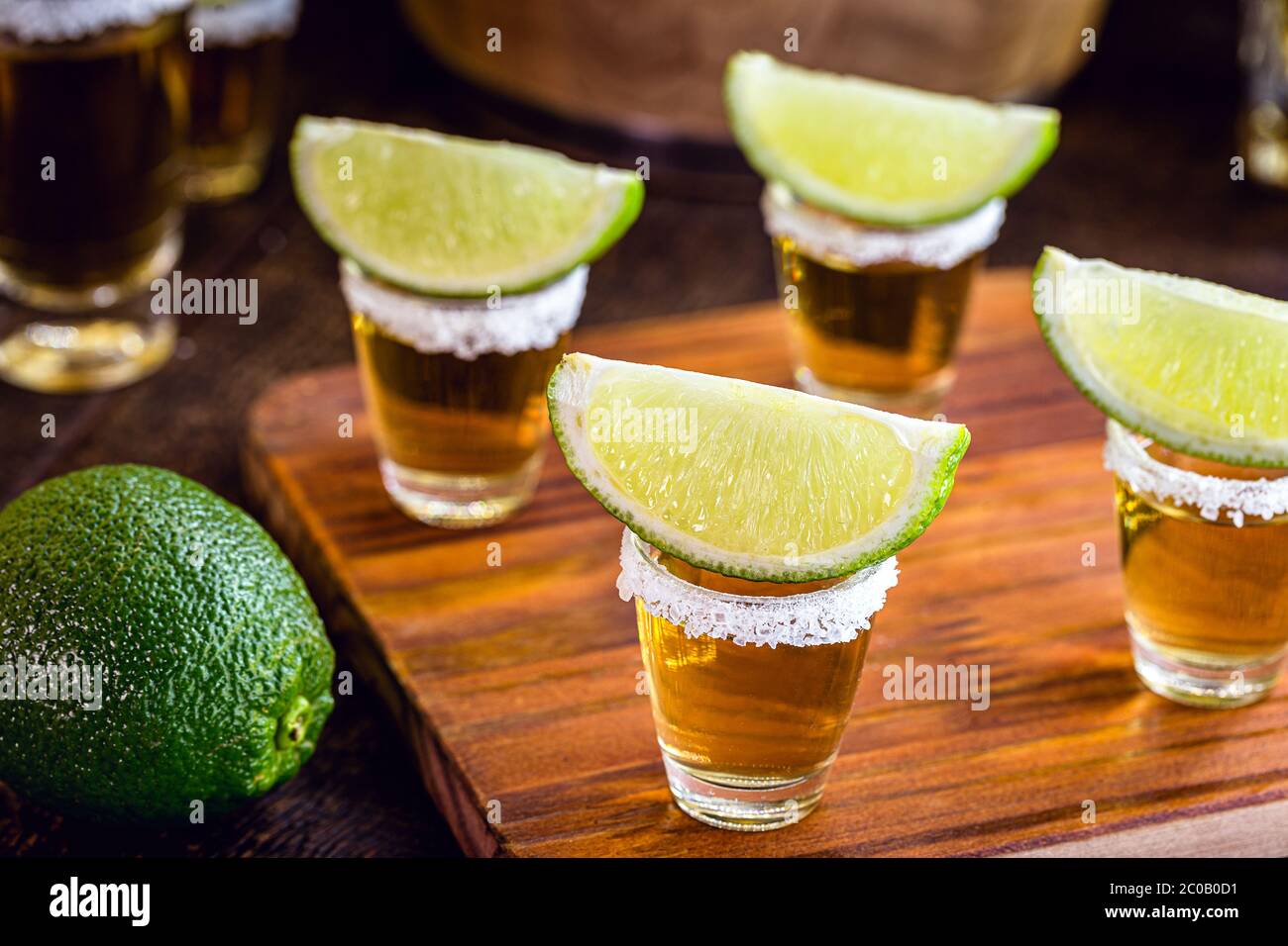 glass of tequila, on wooden table, with lemons and salt in the ...