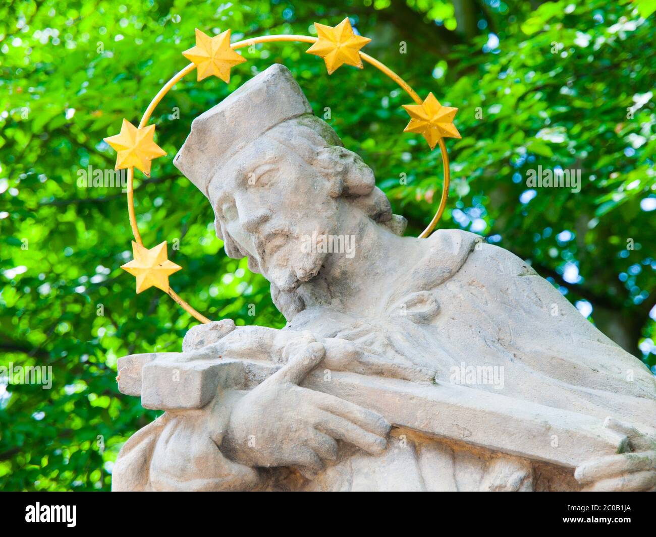 Detailed view of statue of saint with golden halo and green trees on ...