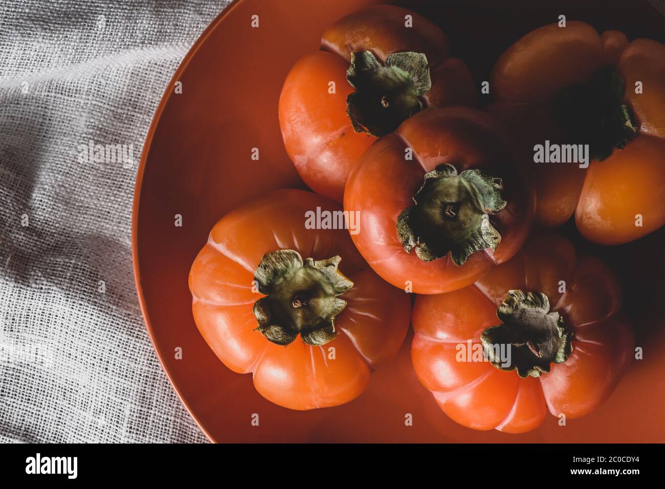 Few fresh persimmons on orange plate Stock Photo - Alamy