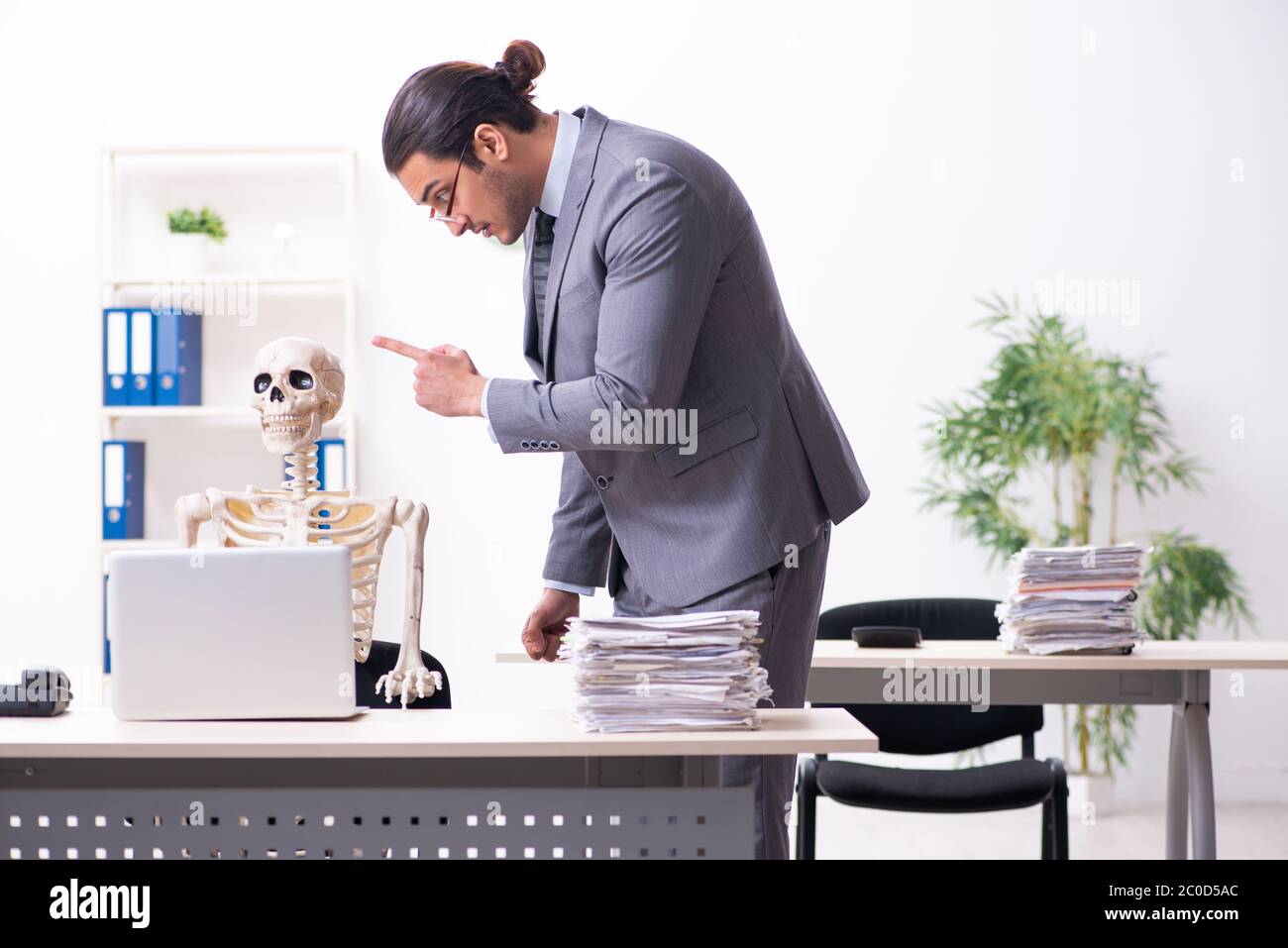 Young employee and skeleton in the office Stock Photo - Alamy