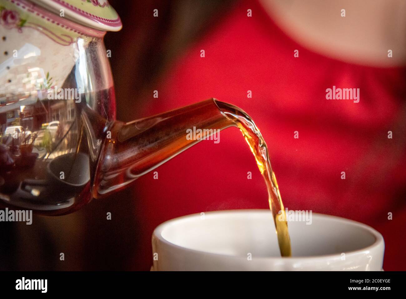 Blurred woman in red pouring tea from a glass teapot Stock Photo - Alamy