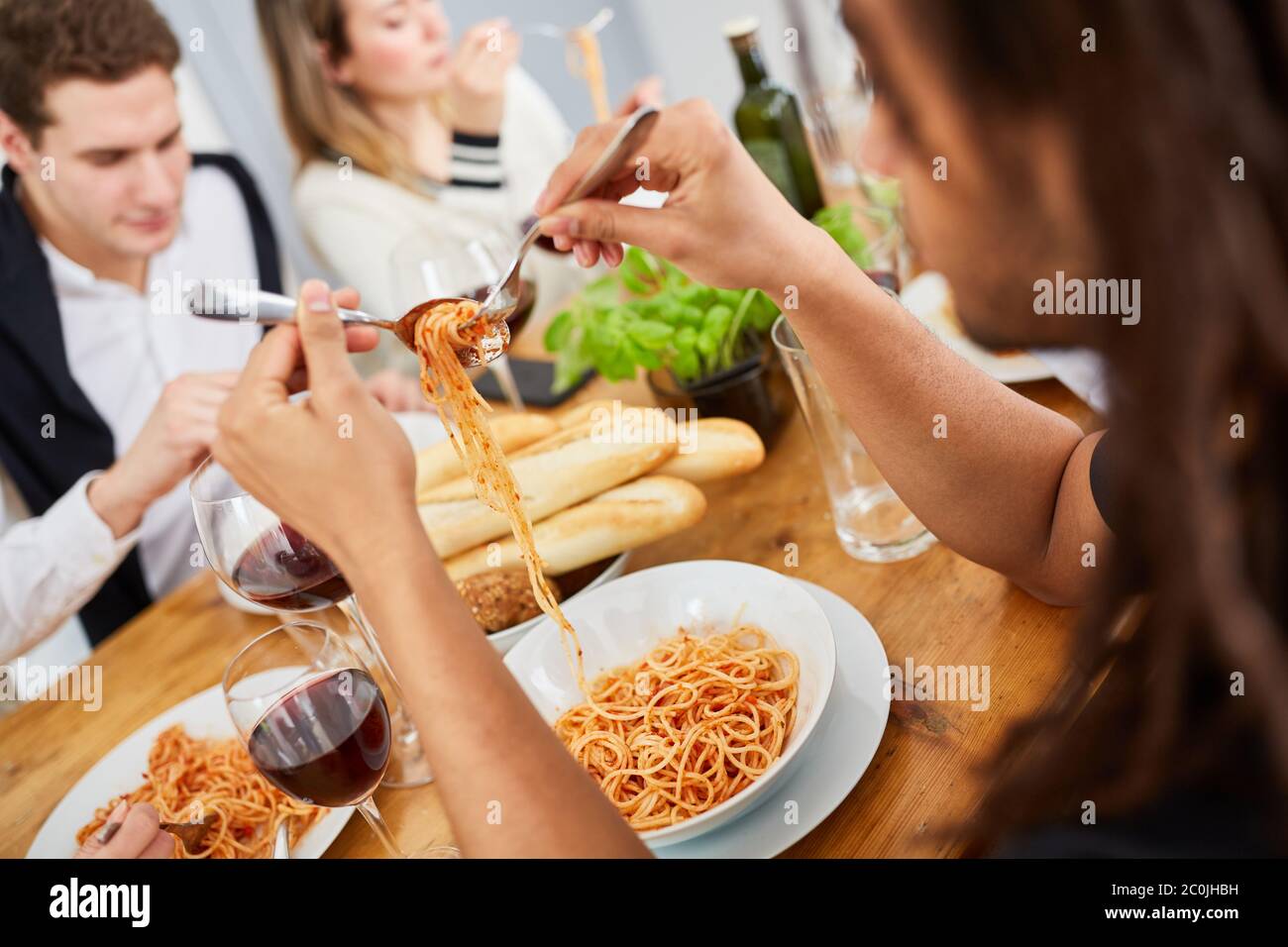 Friends eat spaghetti with tomato sauce together in the kitchen of a ...