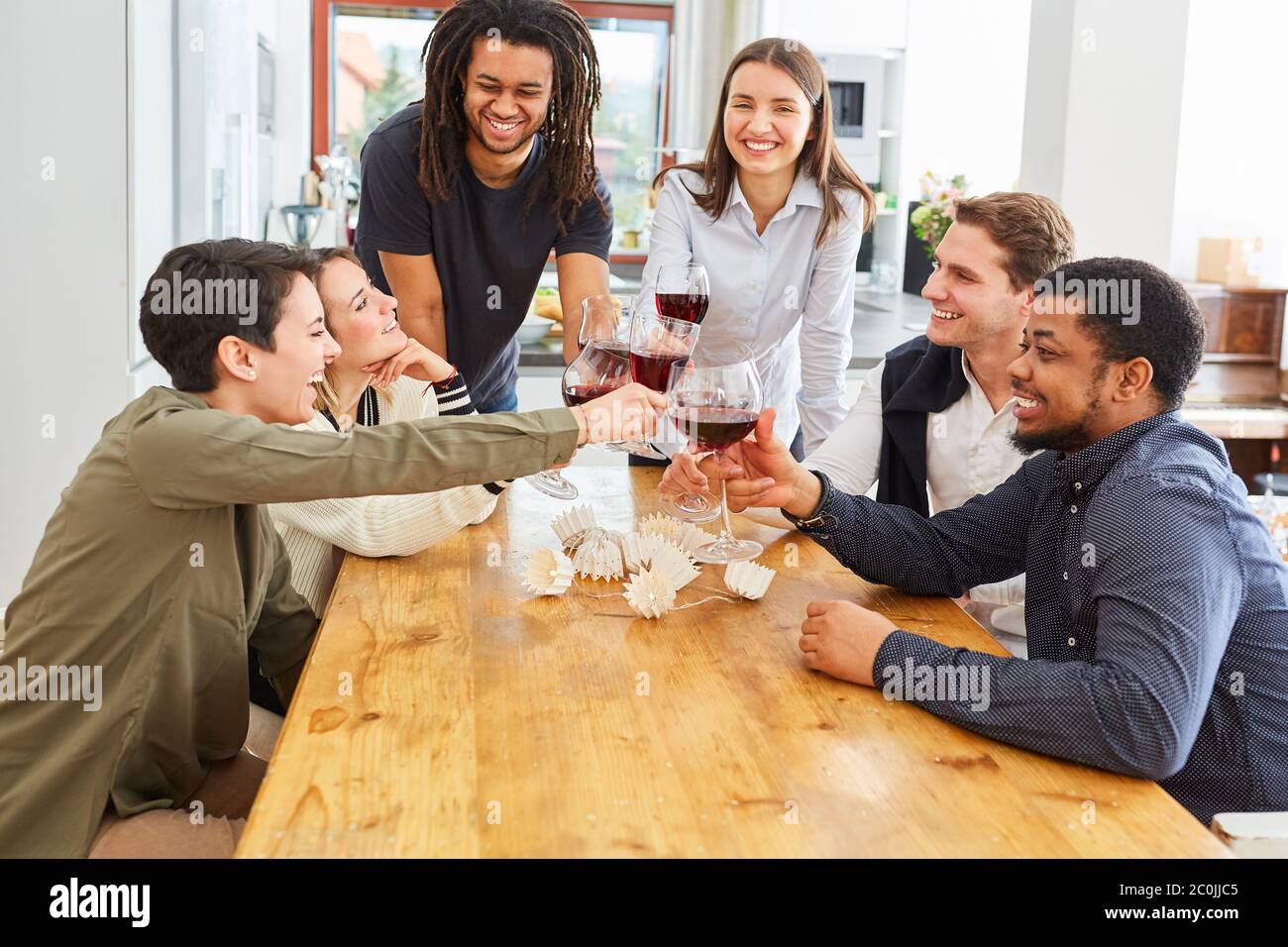 Laughing friends say cheers with a glass of wine at the dining table at ...