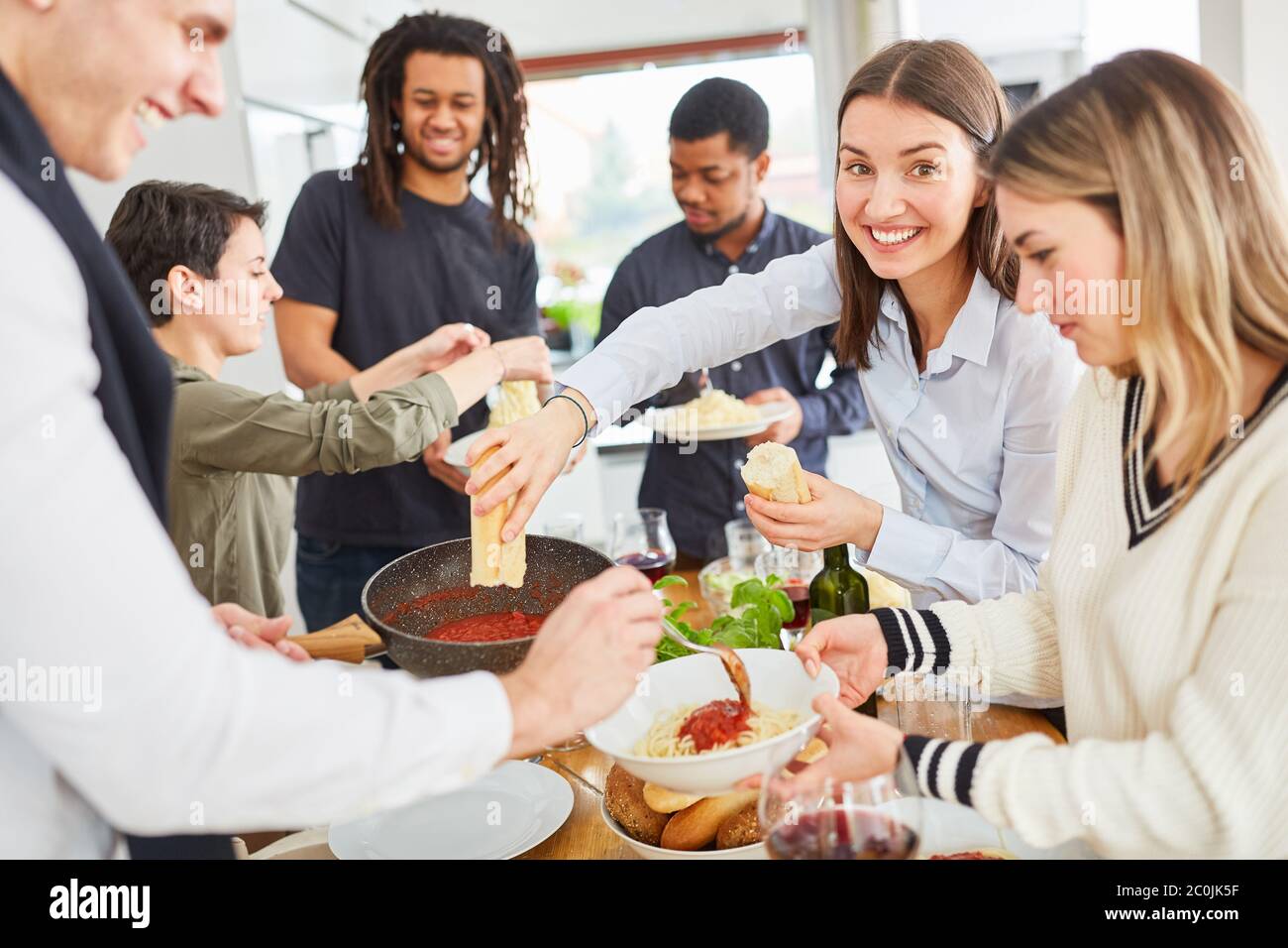 Group of friends serve pasta with tomato sauce with baguette and fresh ...