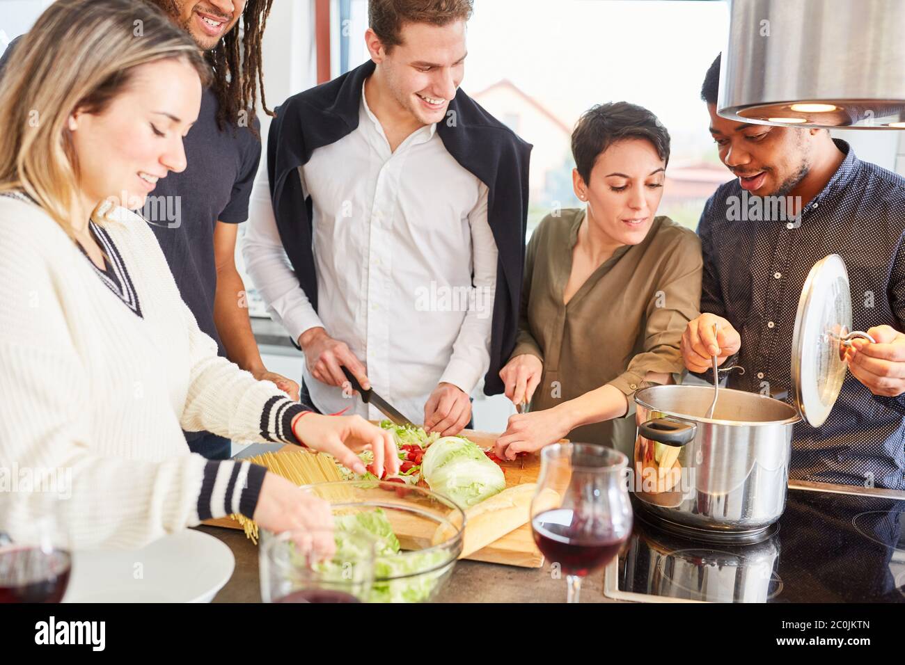 Smiling students and friends prepare meals together in a shared kitchen ...