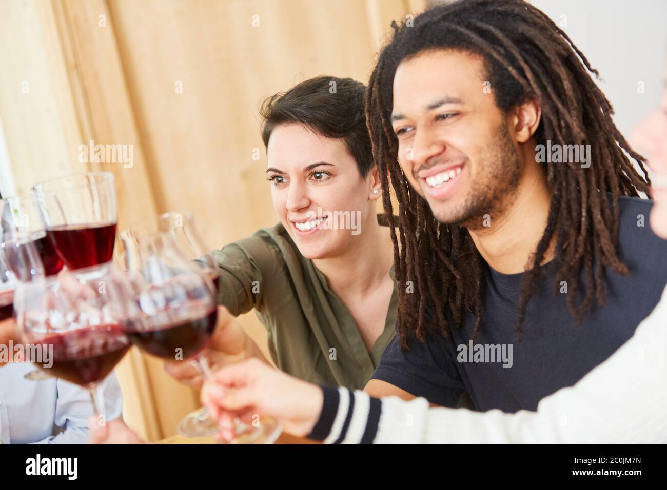 Happy group of friends toasts with glass of red wine at home at ...