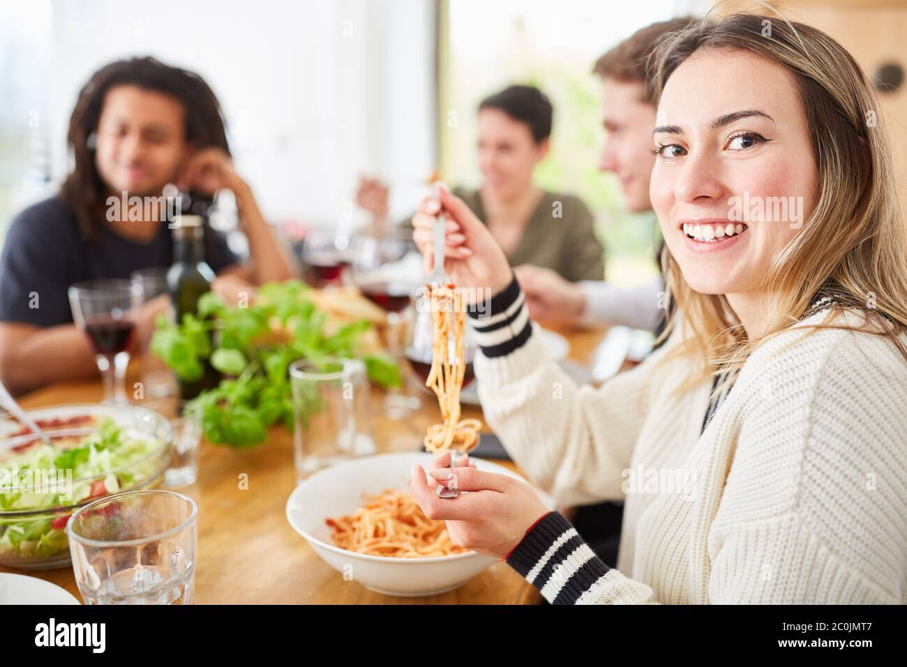 Friends eat spaghetti with tomato sauce together in the kitchen of a ...