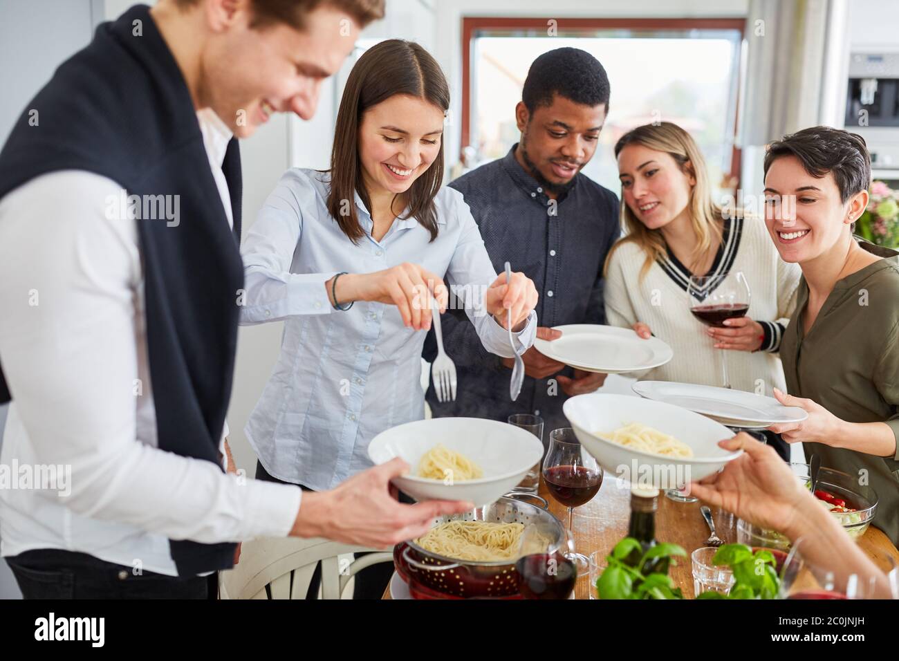 Group of friends having a meal together serving spaghetti in a shared ...