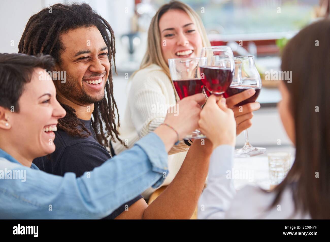 Laughing group of friends clink glasses of red wine together at home in ...