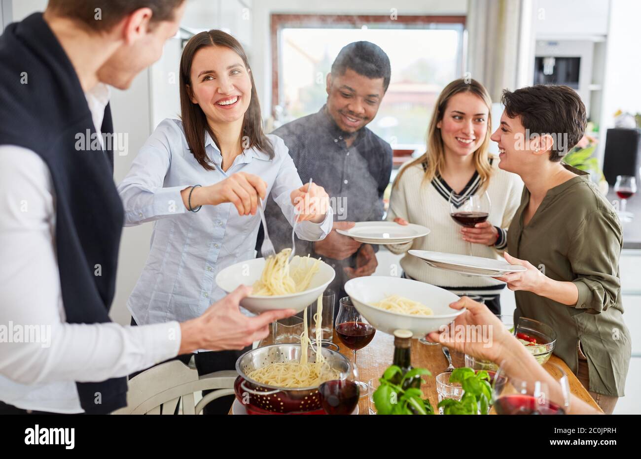 Happy group of friends serve spaghetti for meal together in a shared ...