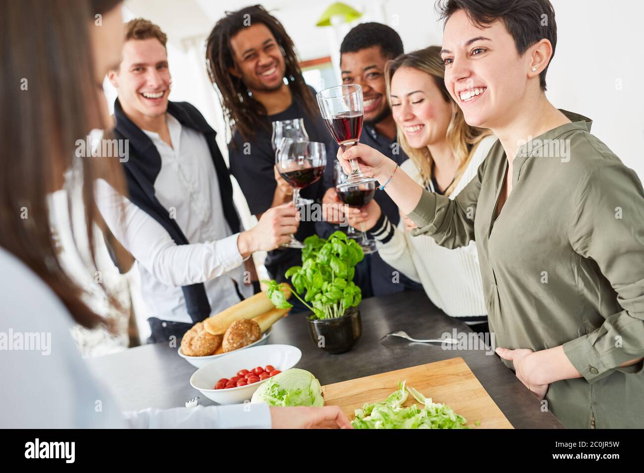 Happy friends toasting with a glass of wine in the kitchen before ...