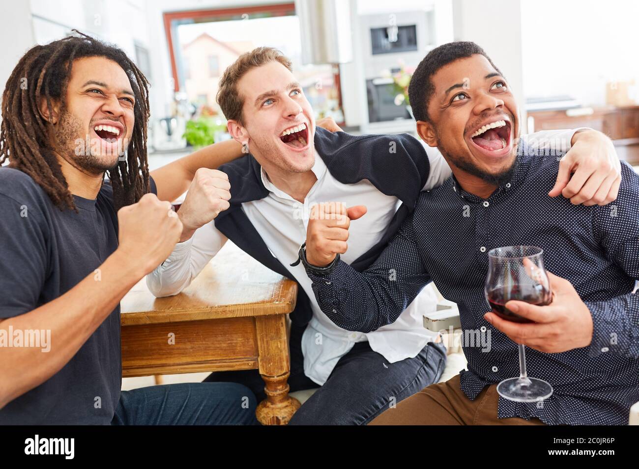 Group of men as friends cheer together while watching football or sport ...