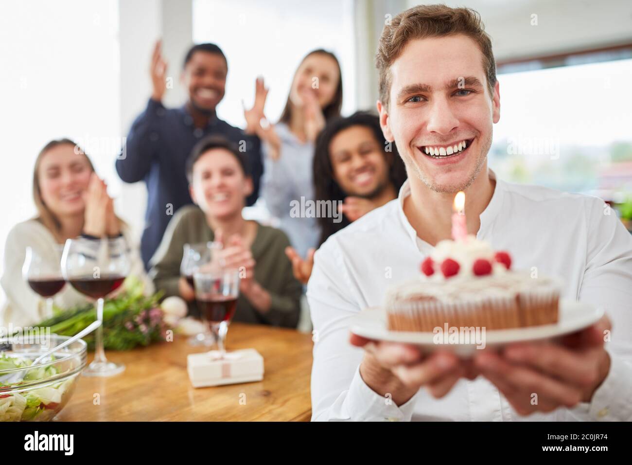 Young man hands birthday cake with candle to friends in the kitchen ...