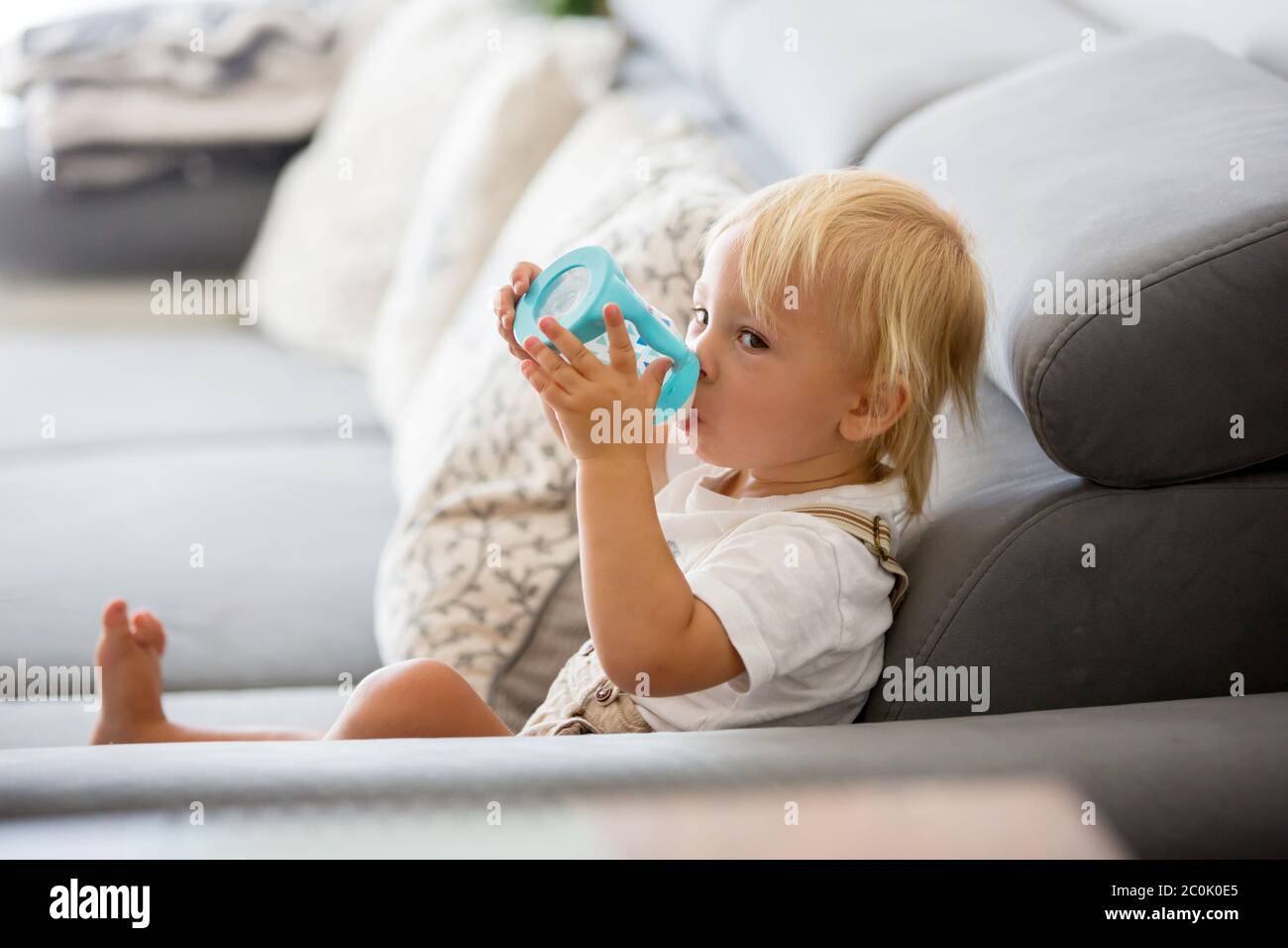 Adorable baby boy drinking milk from a bottle in a white sunny living ...