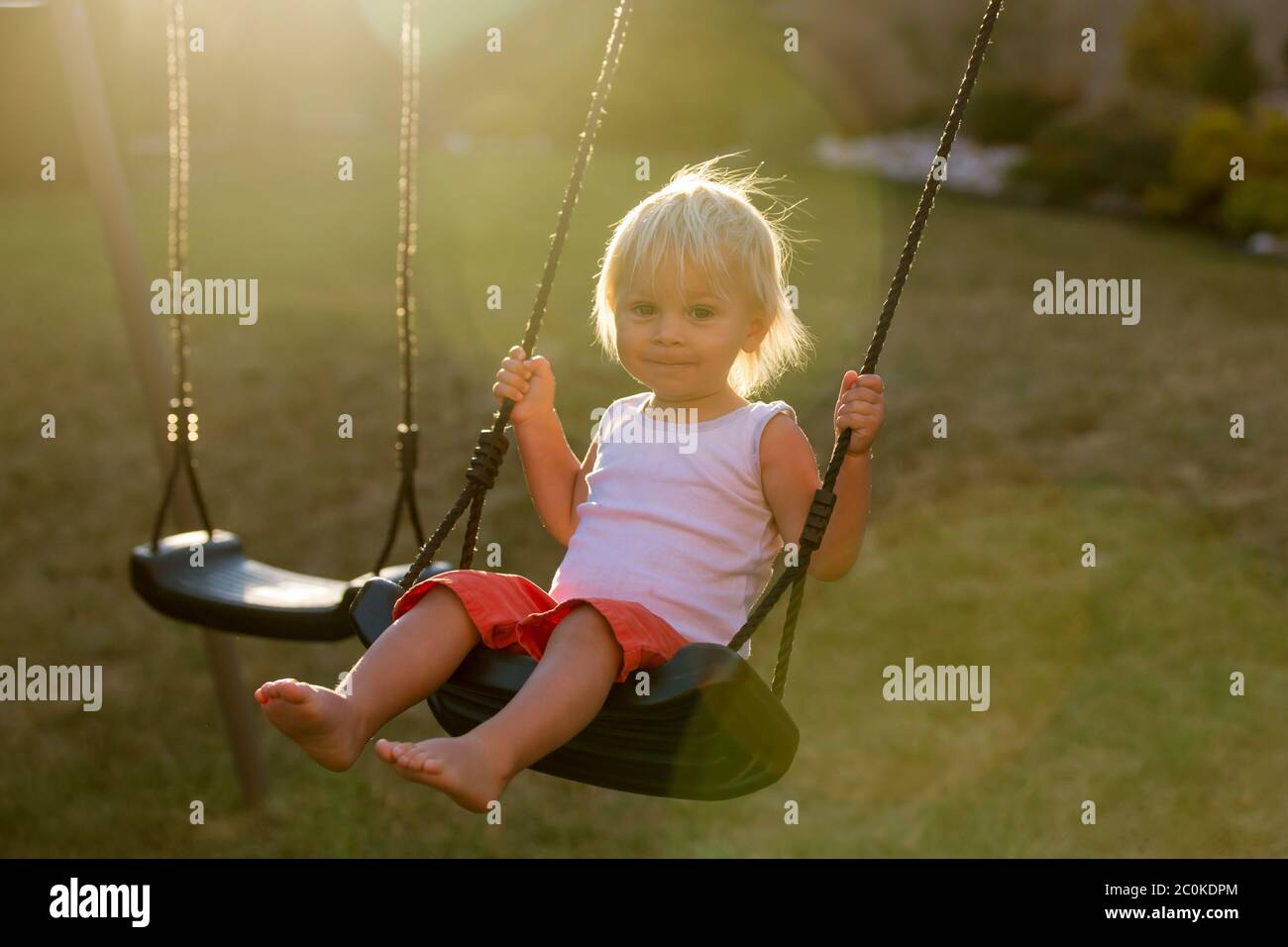 Sweet toddler child, swinging on a swing in garden on sunset, smiling ...