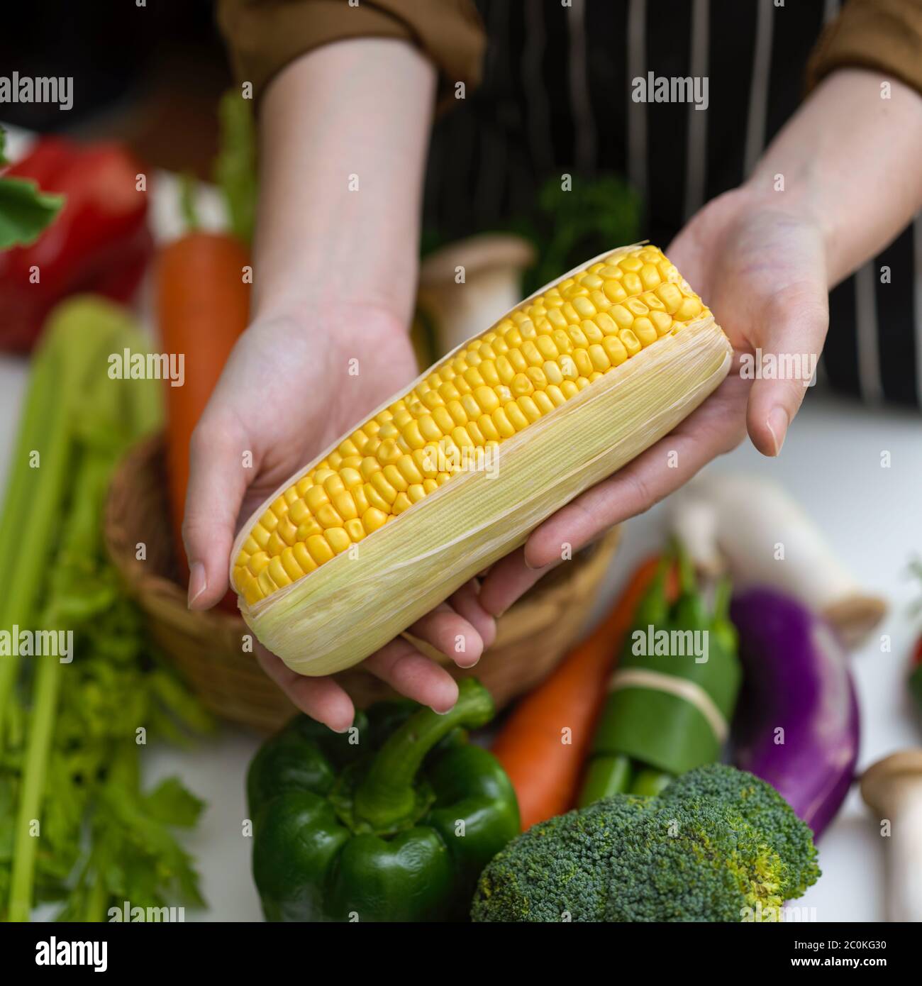 Close up view of hands holding corn on the cob while standing at table ...