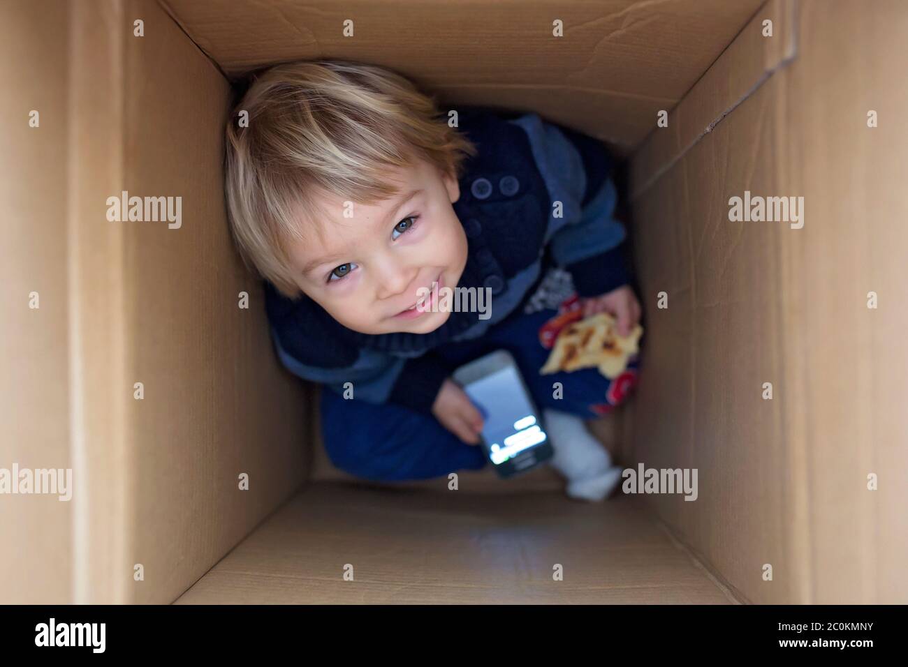 Sweet toddler child, cute blond boy, hiding in cardboard box, looking ...