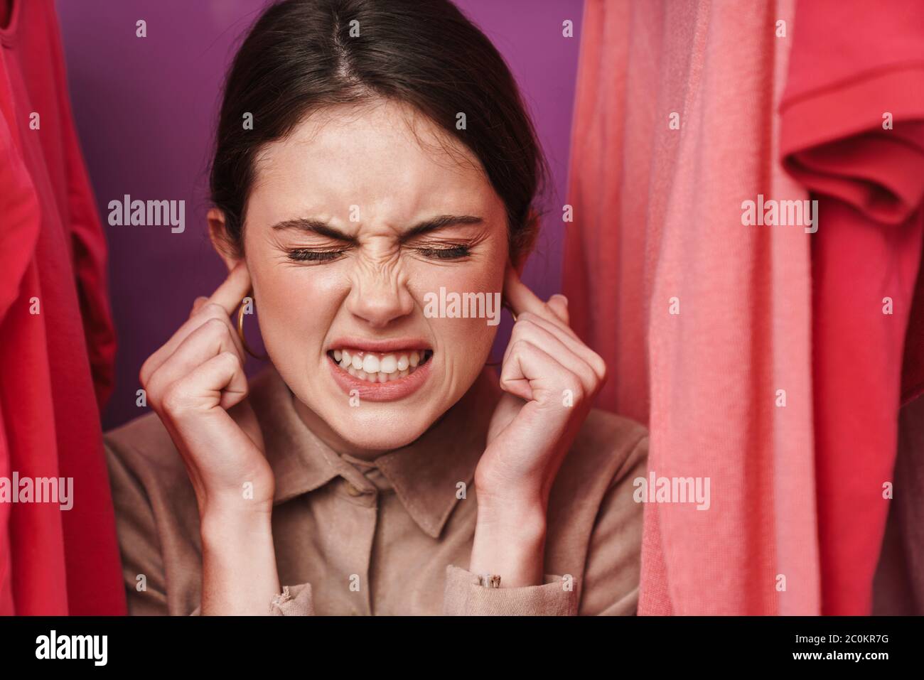 Photo of irritated cute woman plugging her ears while standing at ...