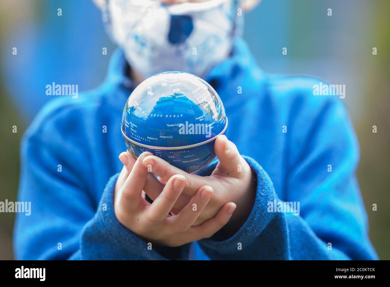School child, holding small globe, looking sad at the world during ...